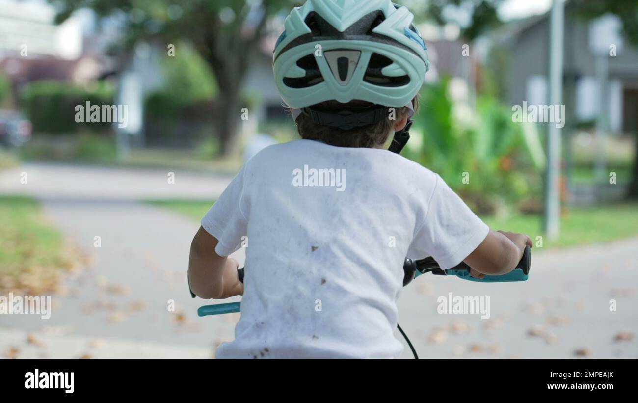 Back of child riding bicycle outside wearing protective helmet. One ...