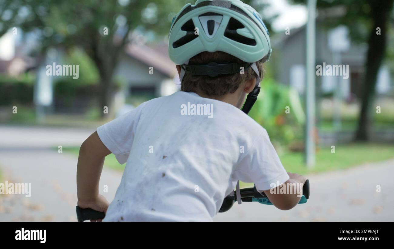 Back of child riding bicycle outside wearing protective helmet. One ...