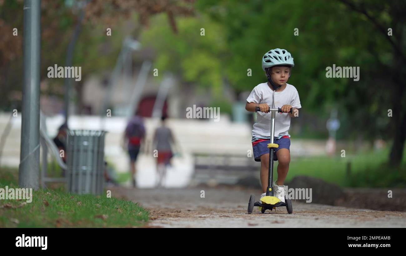 Carefree child riding scooter at park. One male kid wearing helmet ...
