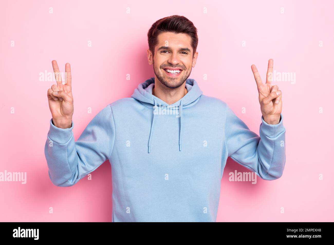 Photo of charming sweet man wear blue hoodie showing two v-signs ...