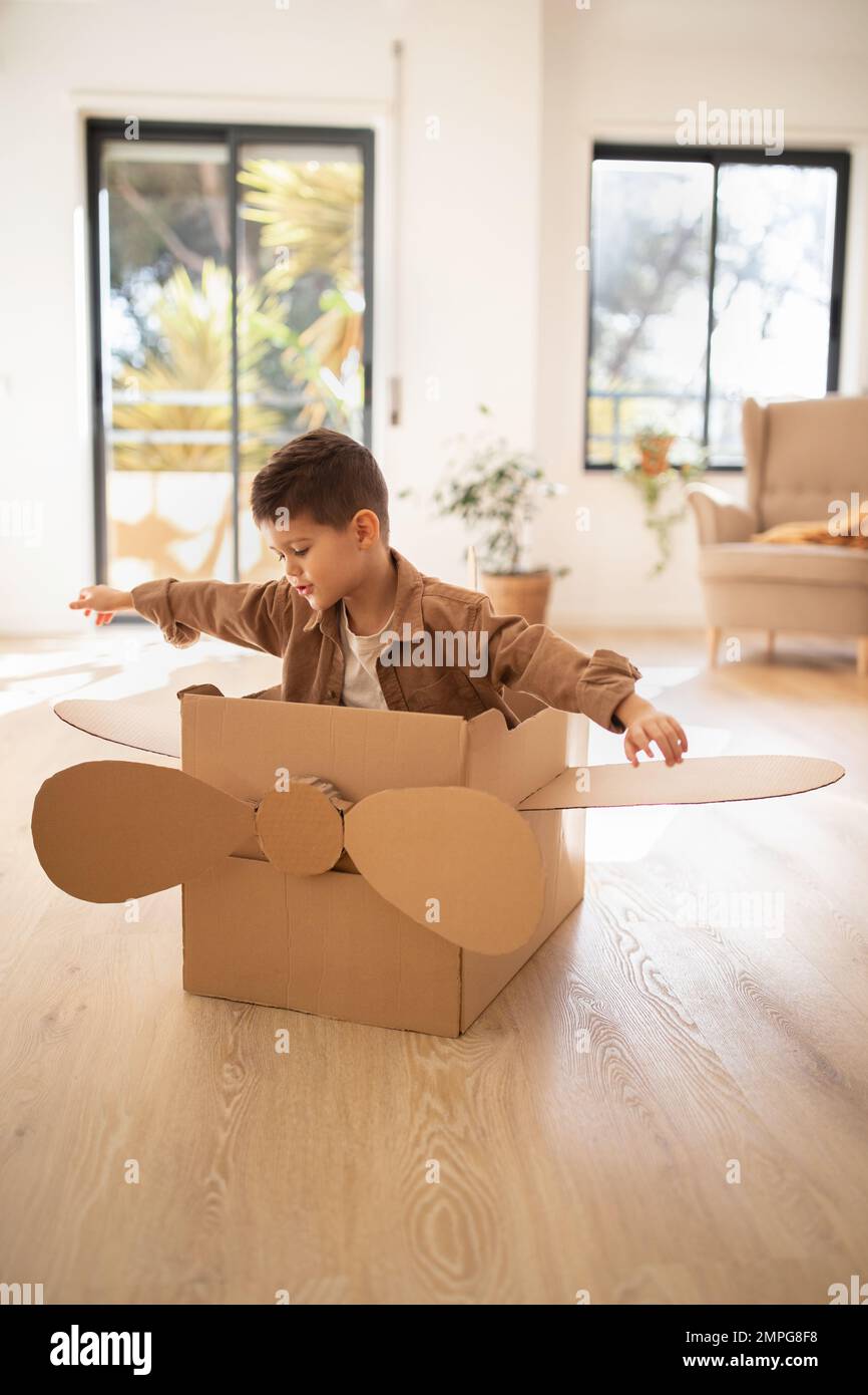 Cheerful small european boy in casual plays in cardboard box helicopter ...