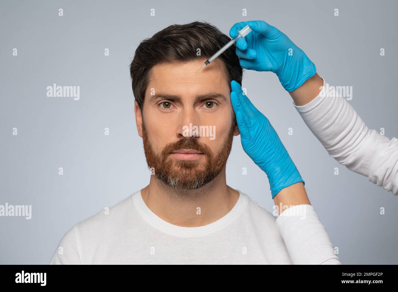 Male patient of beautician receiving filler injection into forehead ...