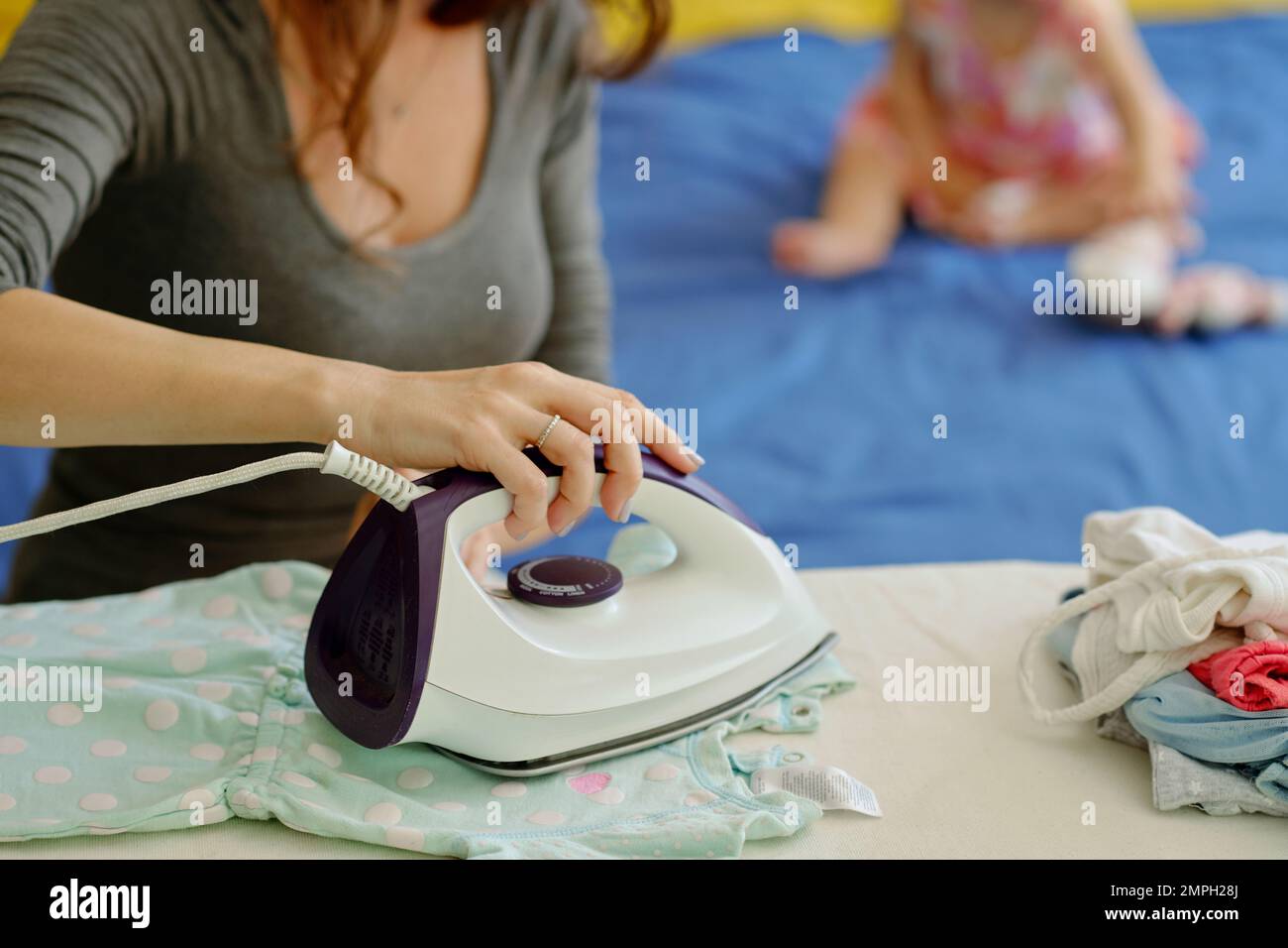 Closeup image of young woman ironing tidy baby clothes after doing laundry Stock Photo - Alamy