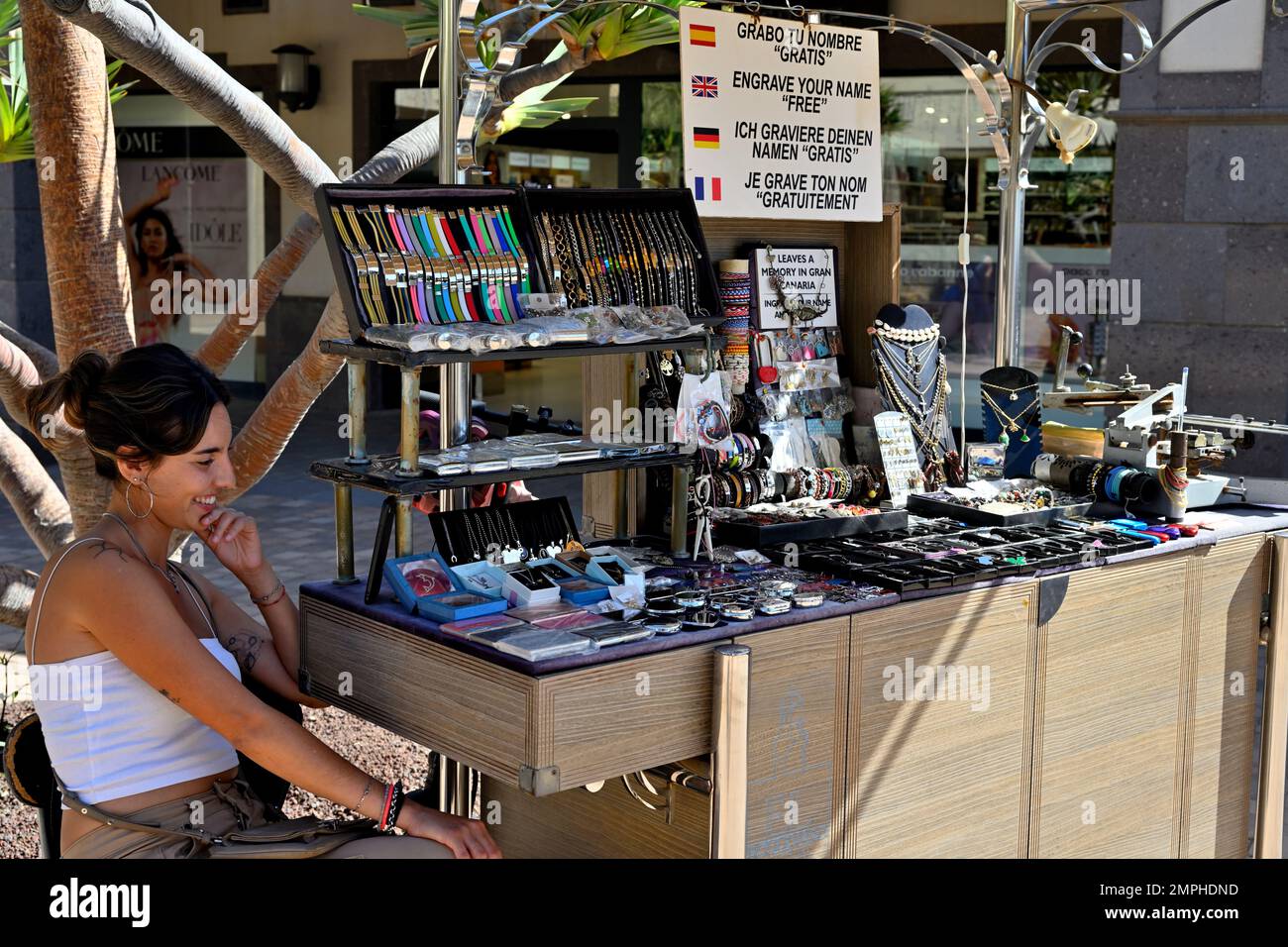 Small craft stall and woman selling jewellery with offer to engrave ...