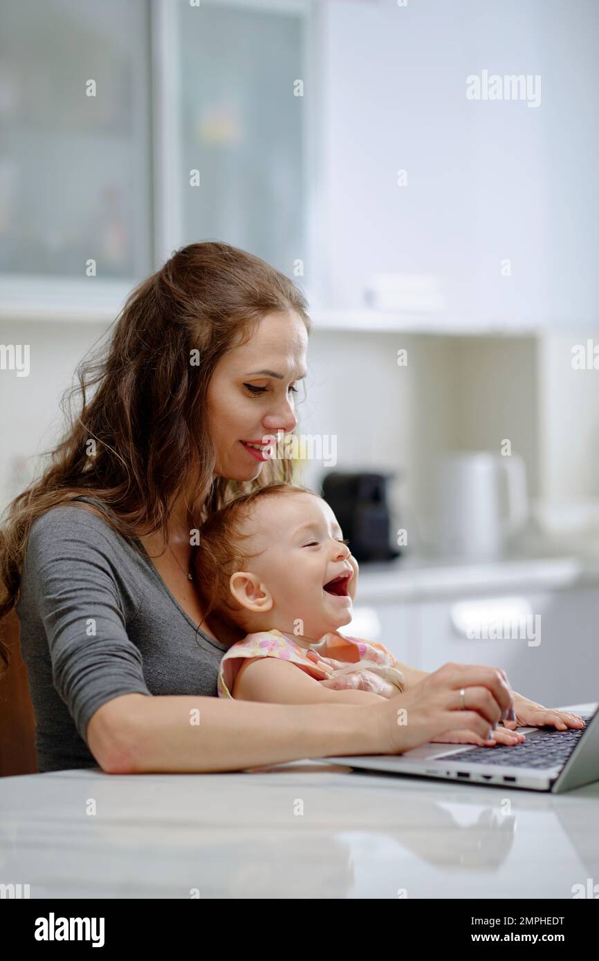 Young woman working on laptop when baby girl sitting on her laptop ...