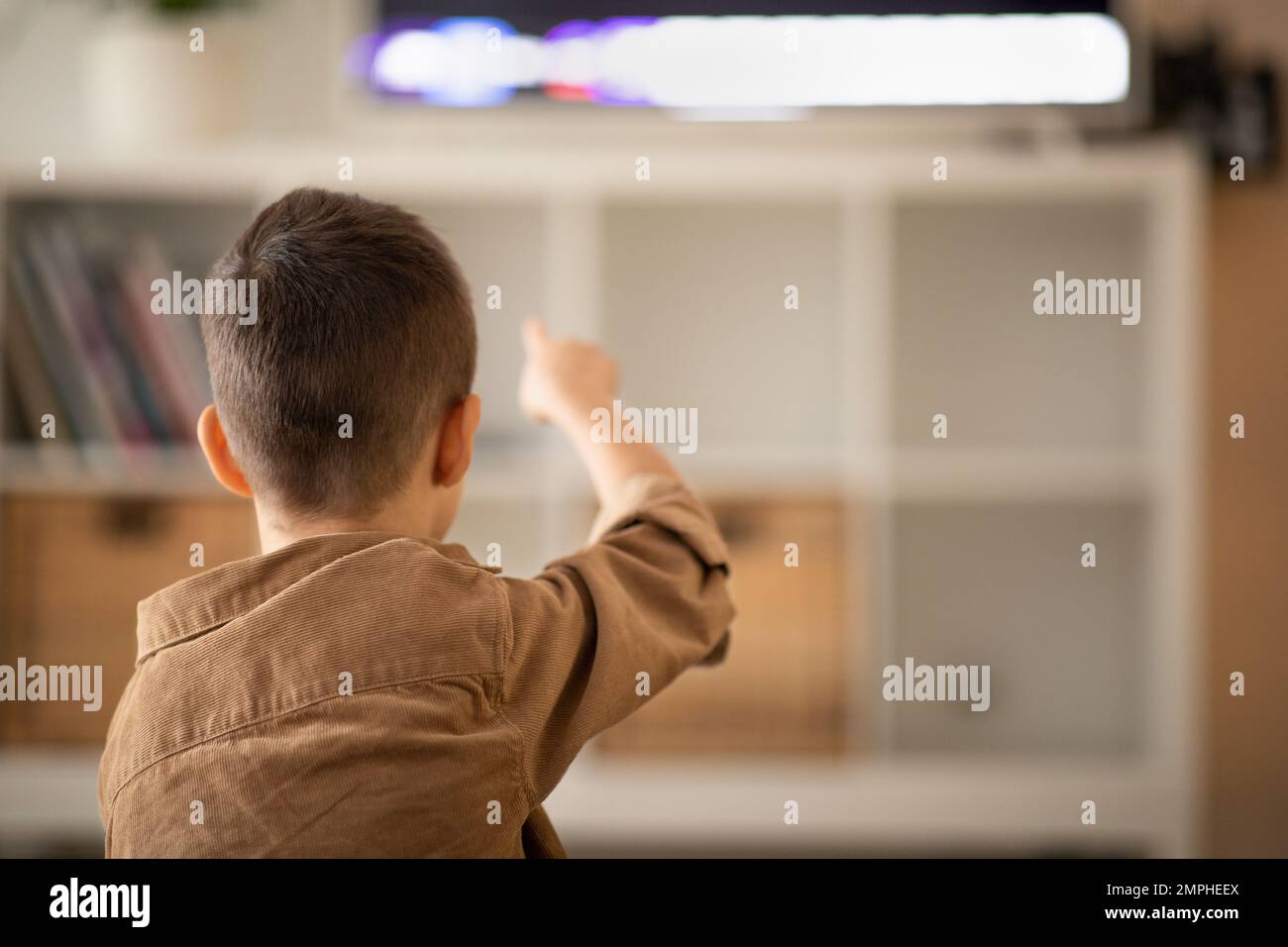 European small kid watch video, pointing finger at tv set, sits on ...