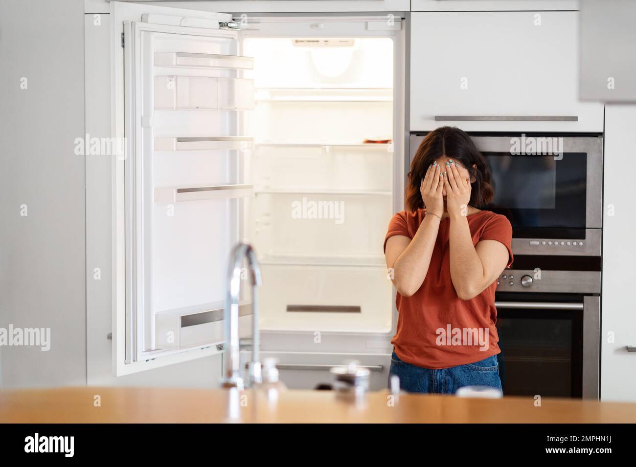 Young Crying Woman Standing Near Open Fridge With No Food In Kitchen ...
