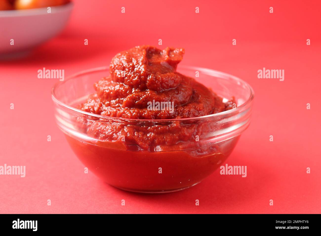 tomato paste in a glass sauce bowl on a red background monocolor. Food ...