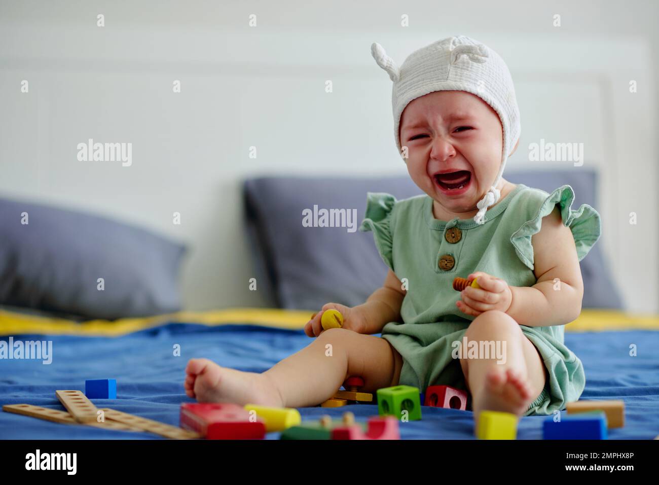 Little girl sitting on bed of parents with many toys and crying Stock ...