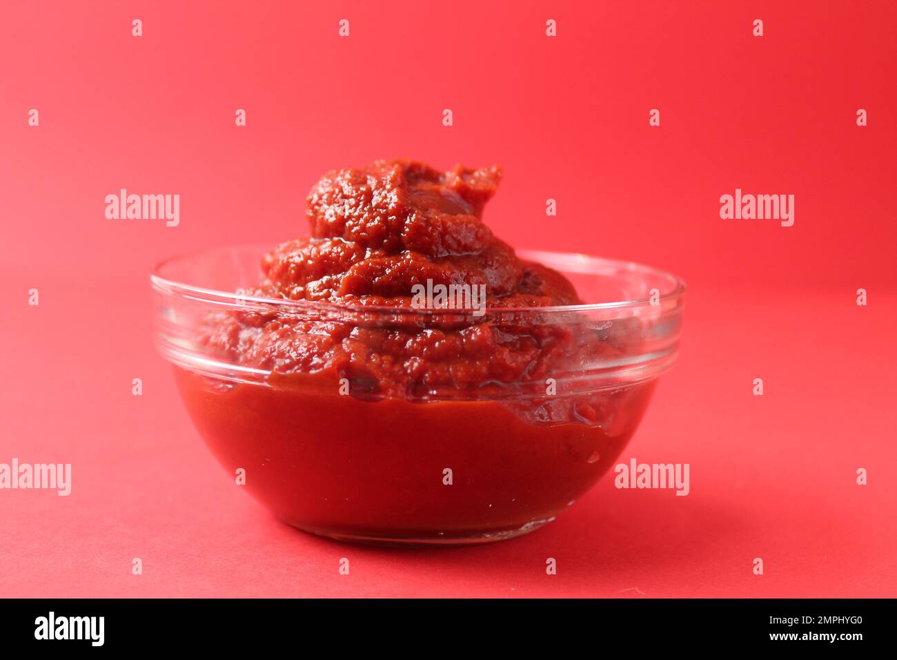 tomato paste in a glass sauce bowl on a red background monocolor. Food ...