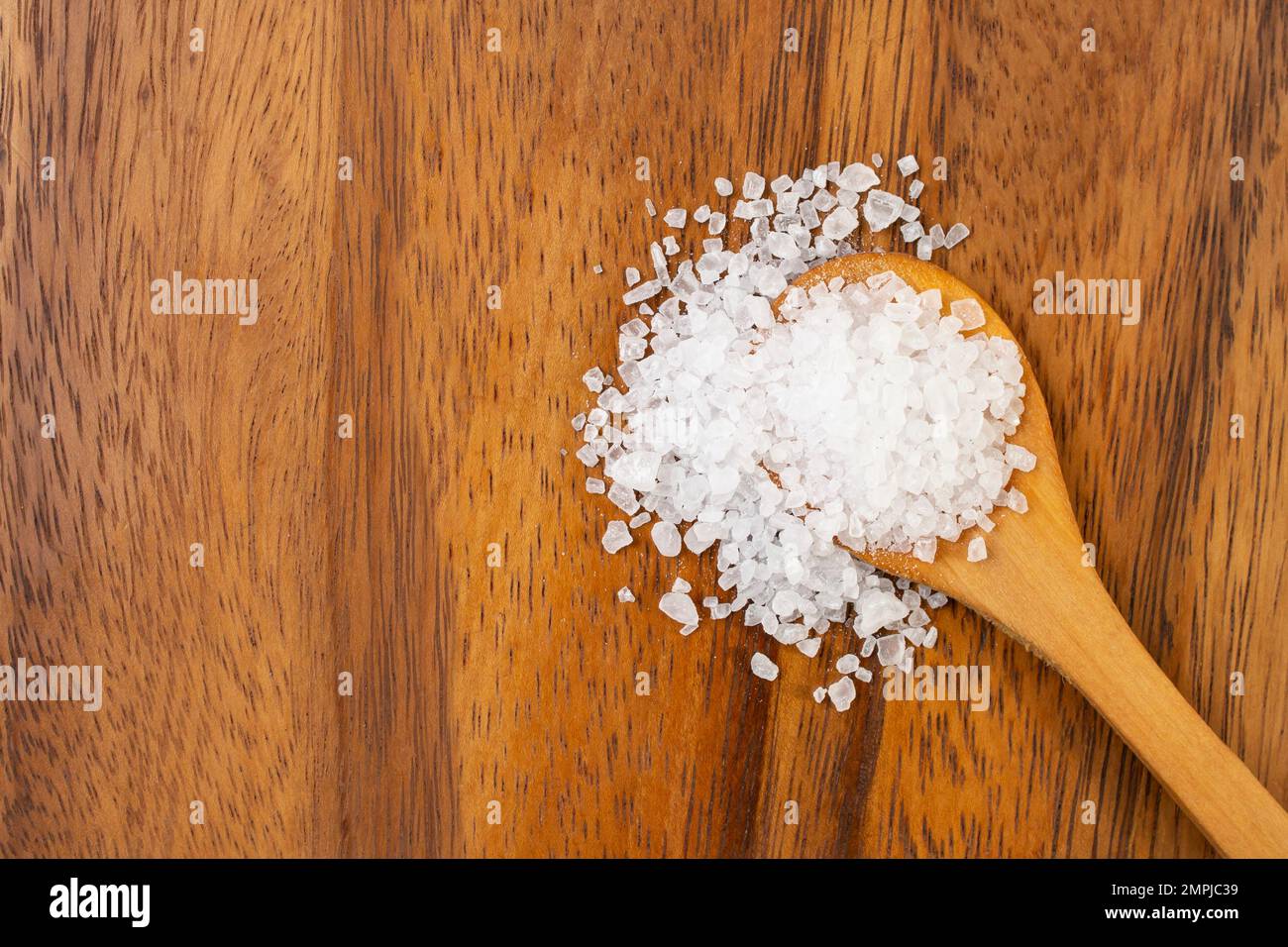 Wooden tea spoon with granulated salt spilling on textured wood ...