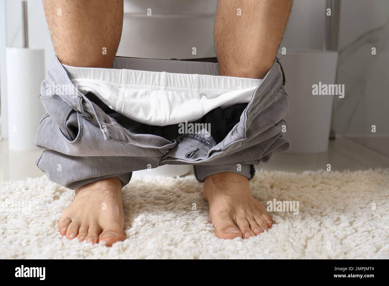 Man sitting on toilet bowl in bathroom, closeup Stock Photo - Alamy