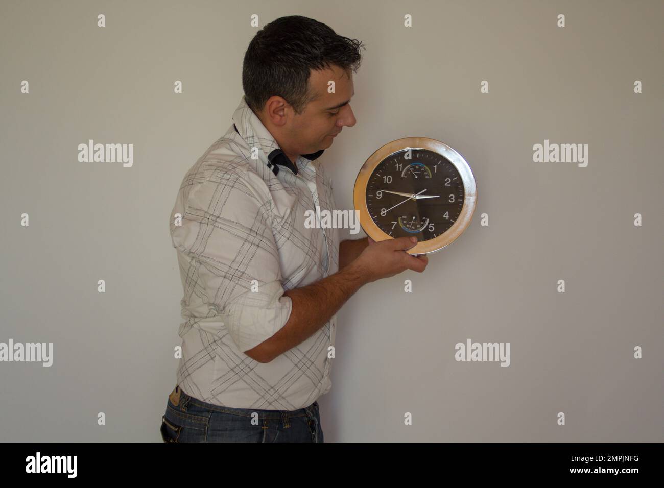 Image of a man holding a wall clock while setting the correct time ...