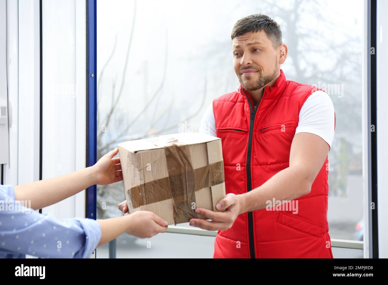 Emotional courier giving damaged cardboard box to client in doorway ...