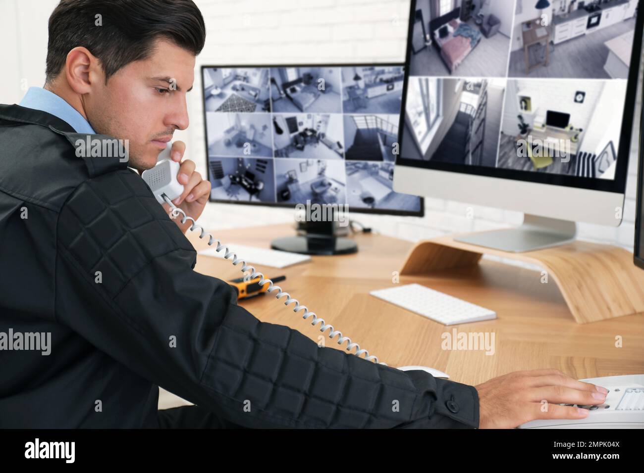 Male security guard talking by telephone near monitors at workplace ...