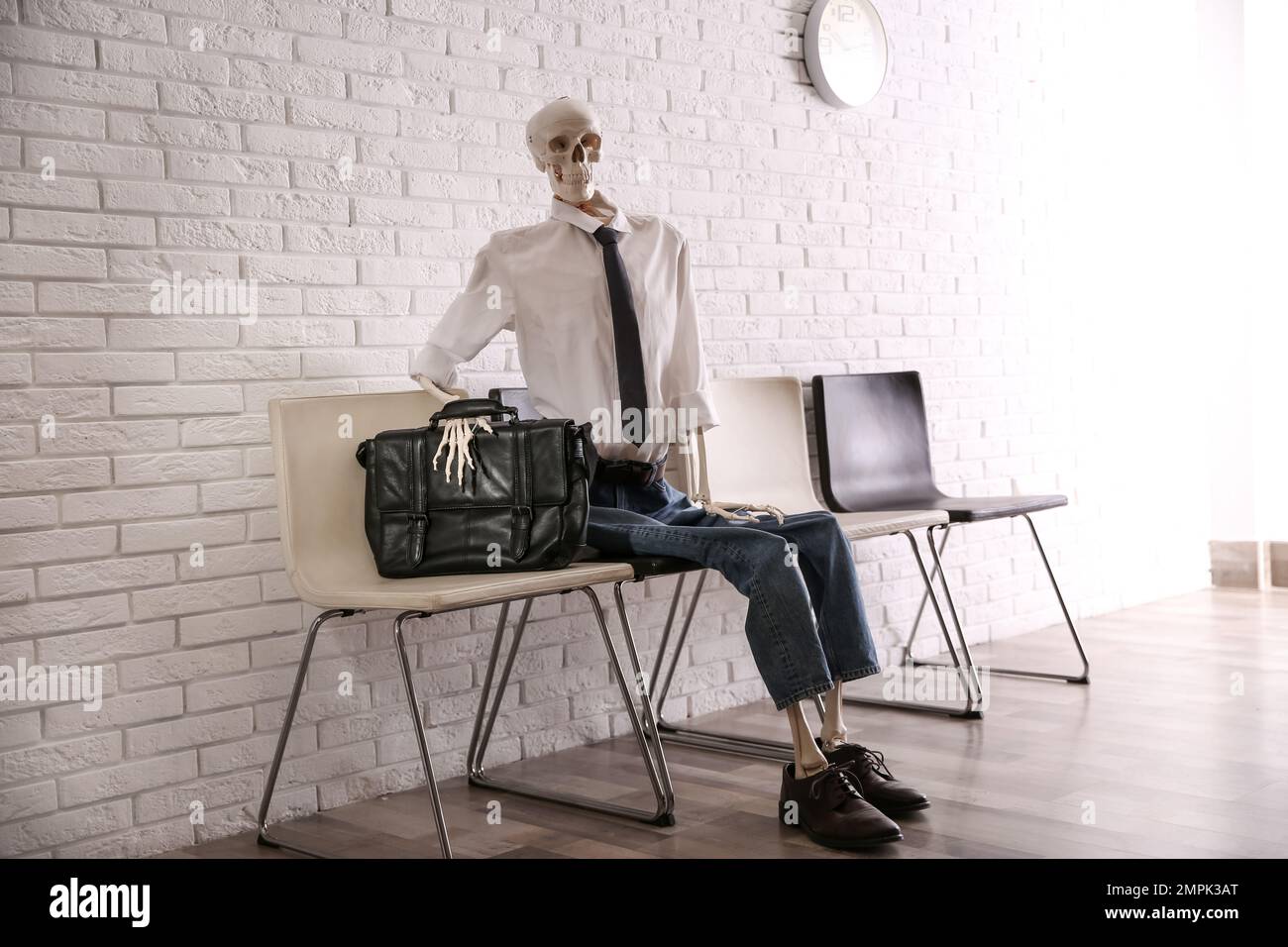 Human skeleton in office wear sitting on chair near brick wall indoors ...
