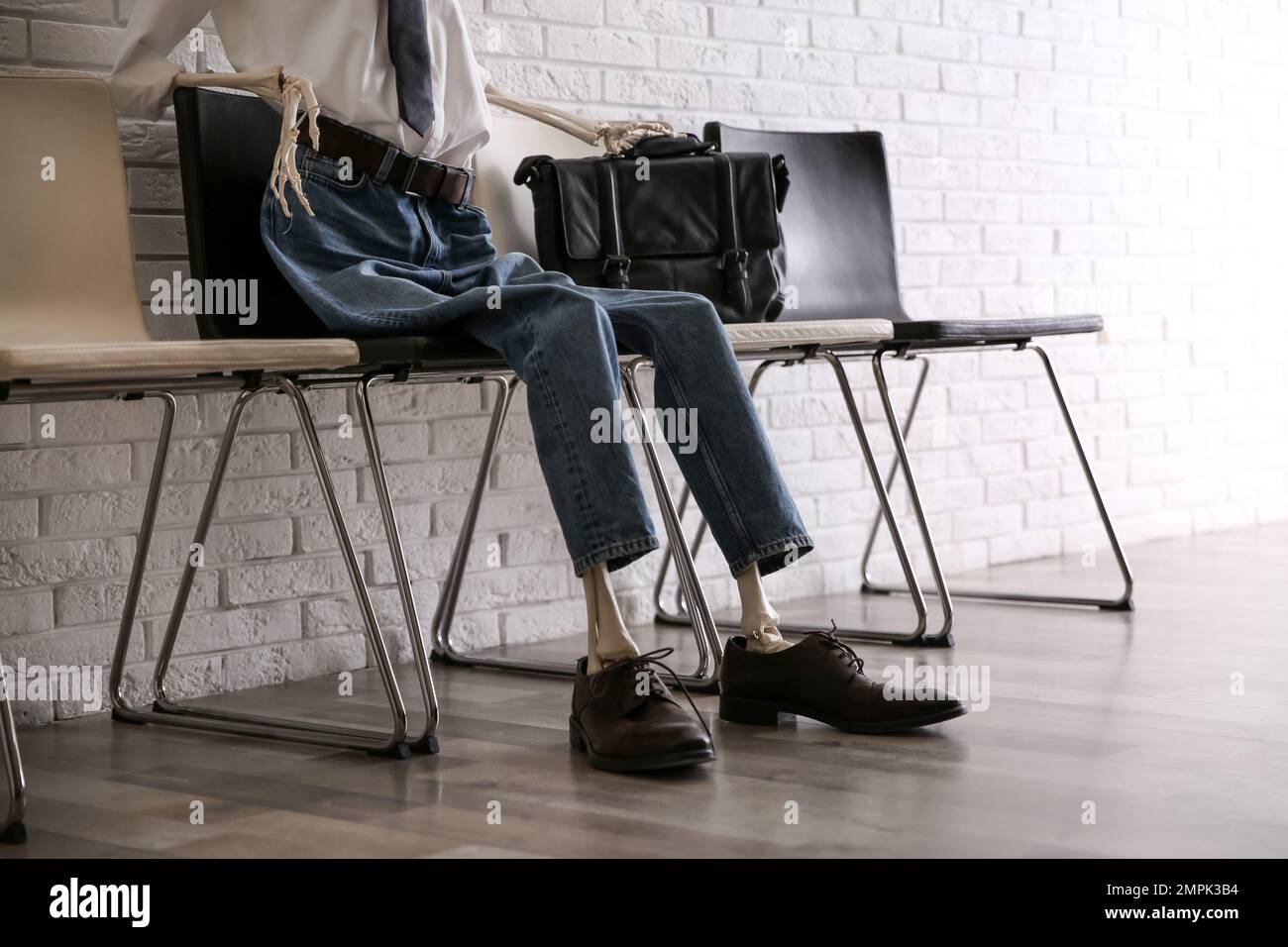 Human skeleton in office wear sitting on chair near brick wall indoors ...