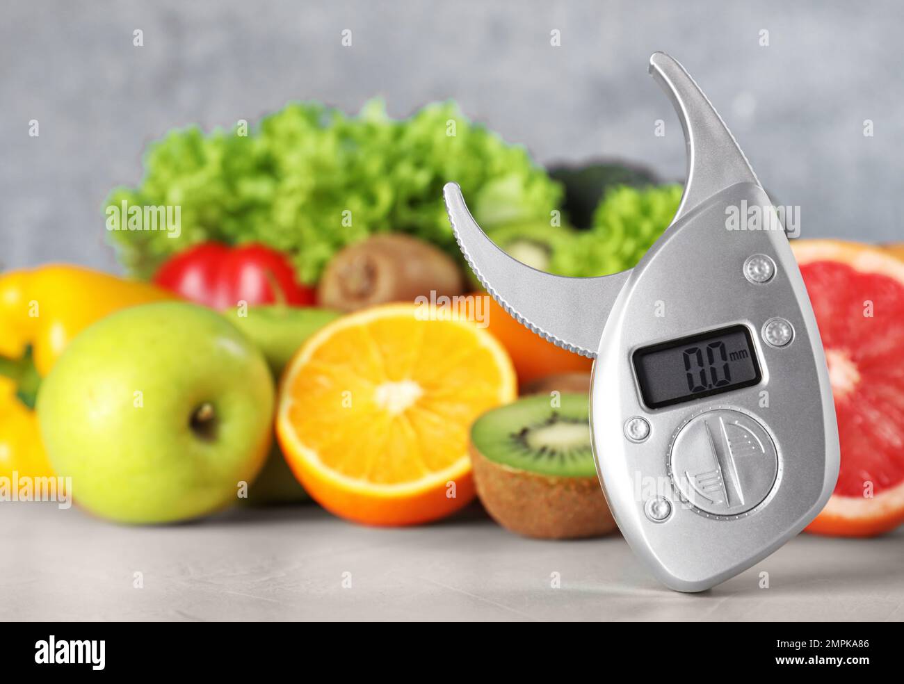 Digital body fat caliper, vegetables and fruits on table. Diet plan ...