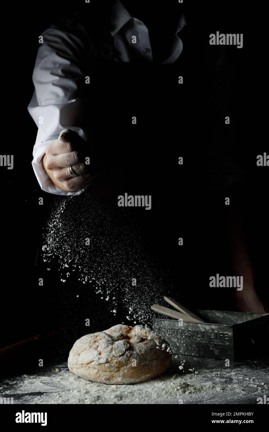 Unidentified woman hand sprinkle, pouring flour to fresh bread on black ...