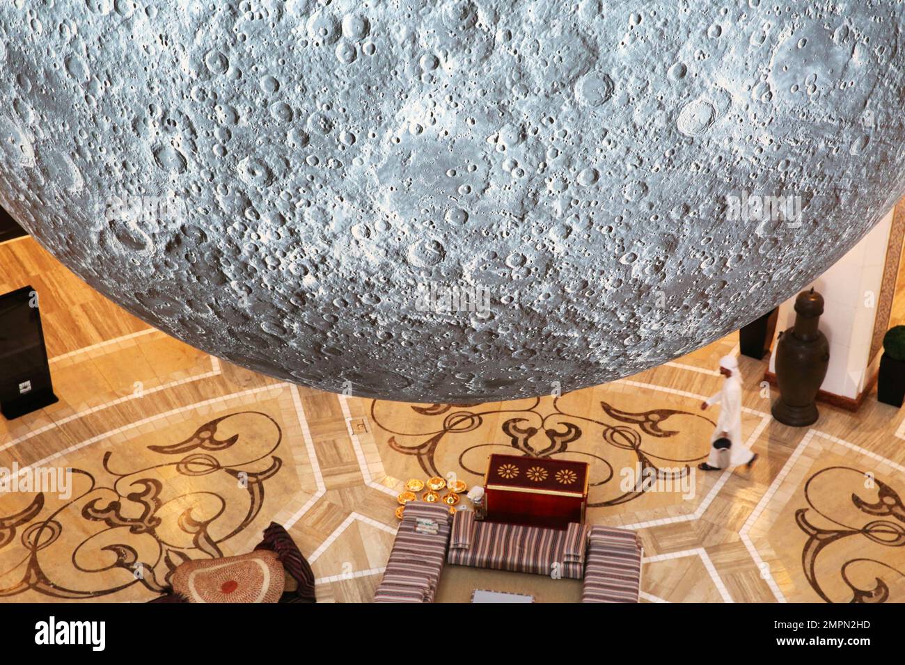 An Emirati in traditional robes walks underneath a giant model of the ...