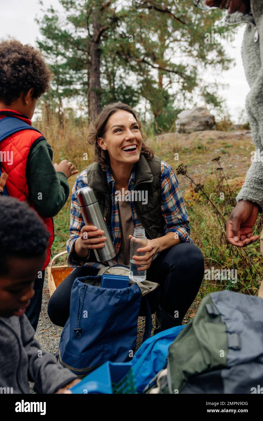 Happy woman unpacking bags while crouching by family during vacation ...