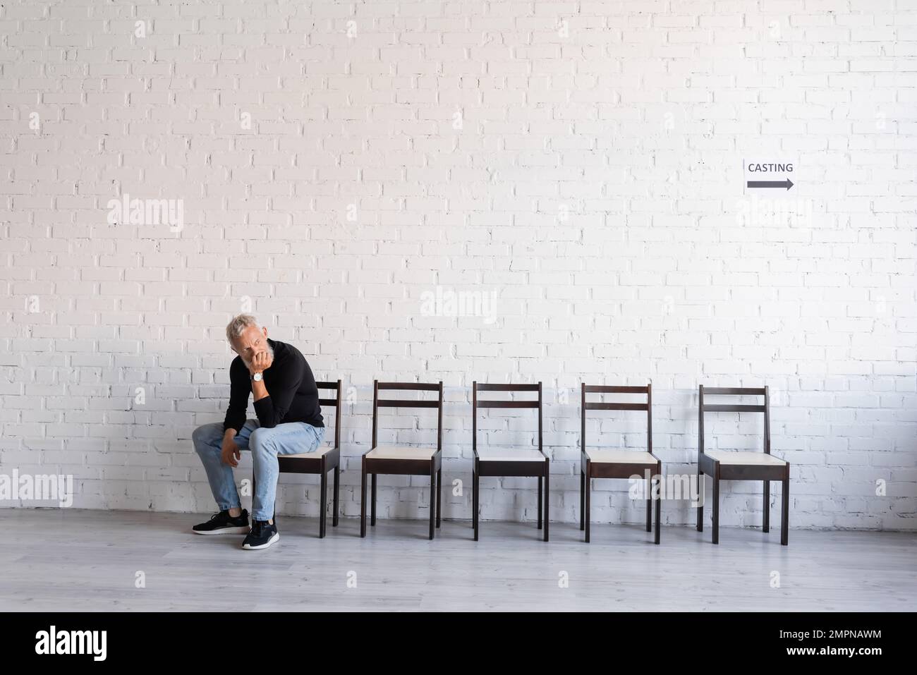 grey haired middle aged actor sitting on chair in corridor and waiting ...