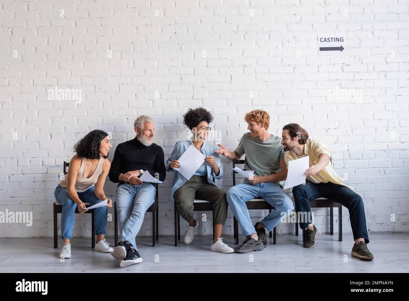 redhead man pointing with hand while talking to multicultural actors ...