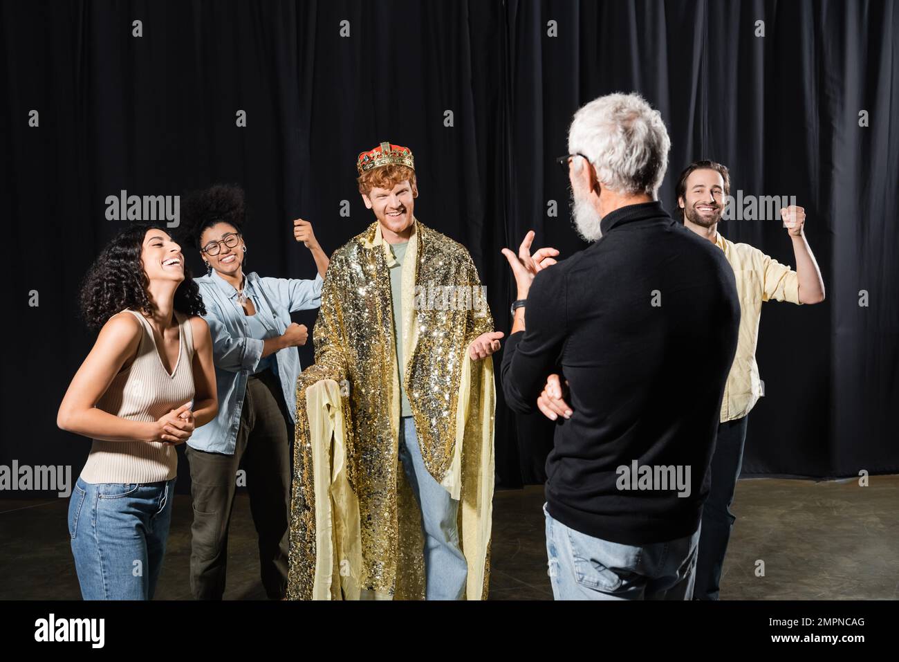 cheerful redhead man in king costume near multiethnic actors and art ...