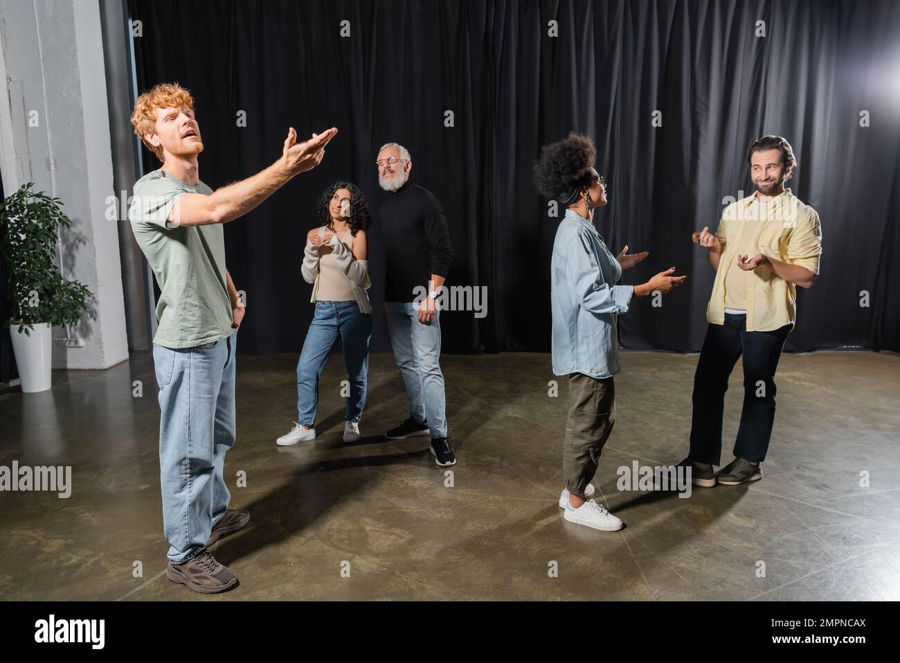 redhead man rehearsing with outstretched hand near art director and ...