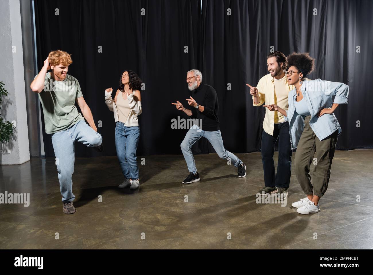 cheerful multicultural actors pointing at redhead man rehearsing on ...