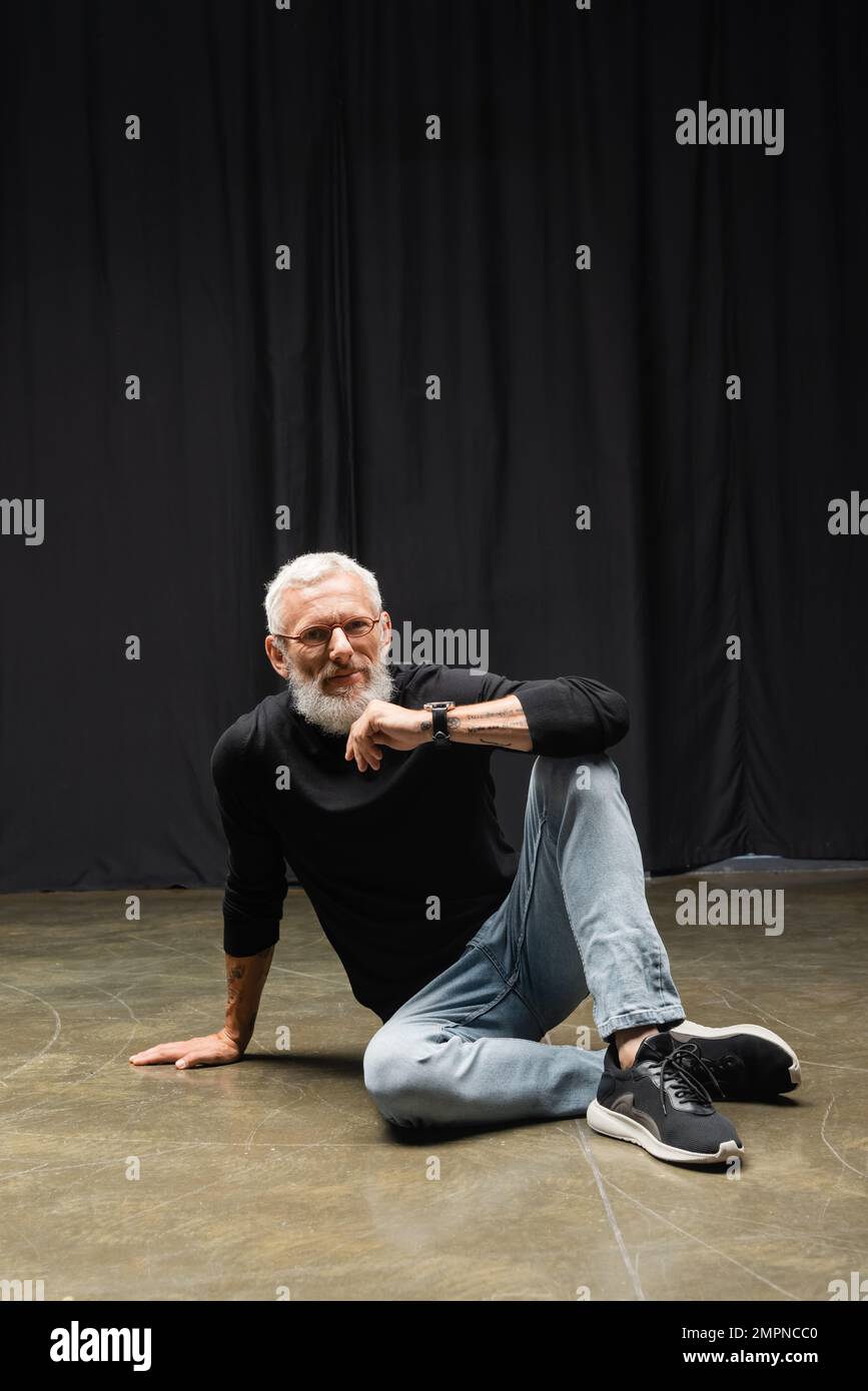 tattooed and bearded actor sitting on theater stage. Translation of ...