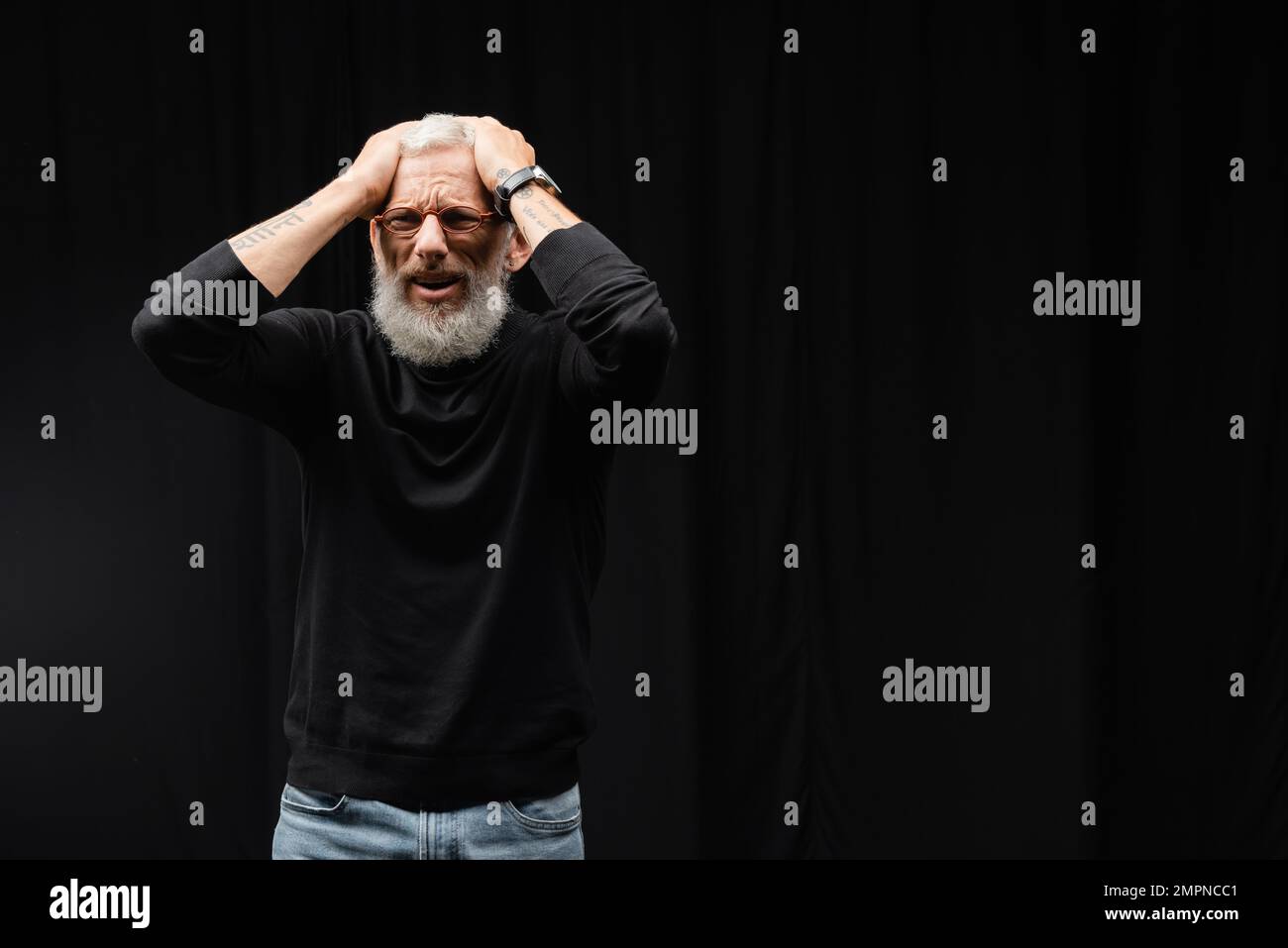 tattooed actor with depressed face expression touching head while ...