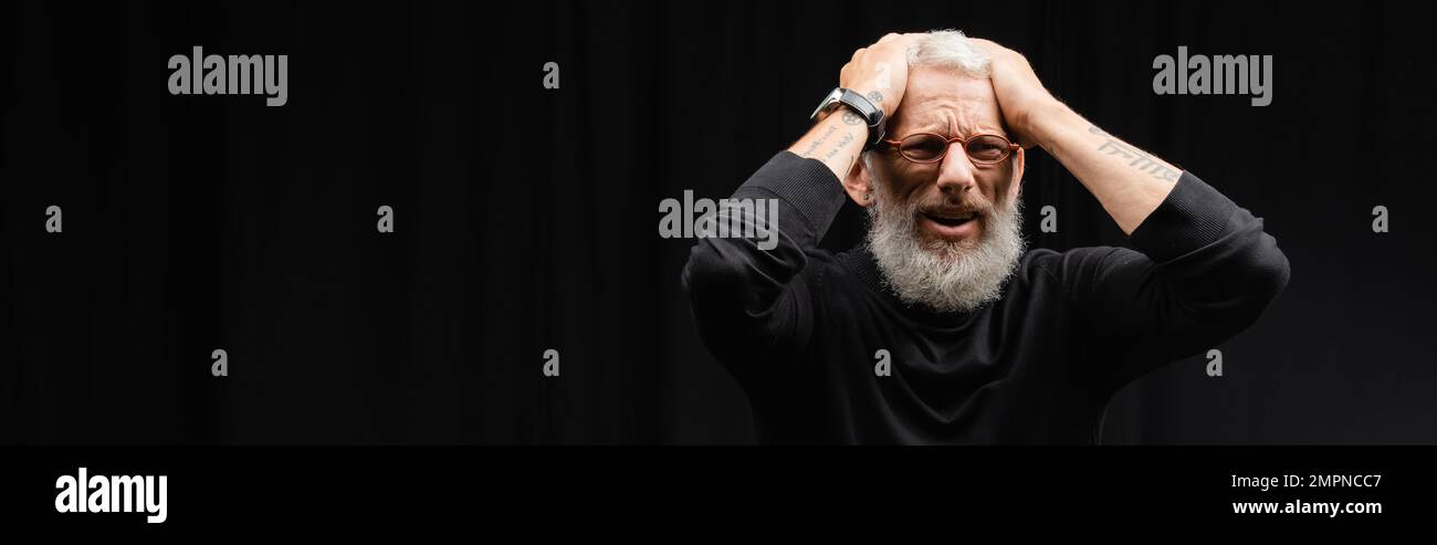 frustrated tattooed actor holding hands on head while playing dramatic ...