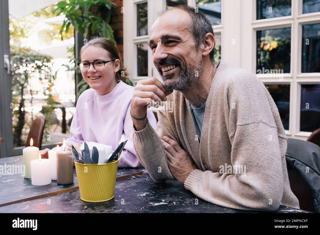 Happy father with hand on chin sitting by daughter on dining table at ...