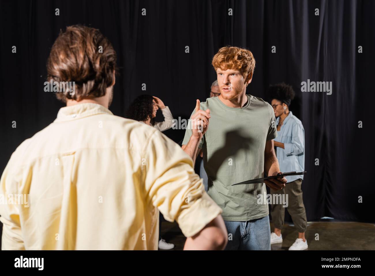 redhead actor holding clipboard and pointing with finger near blurred ...