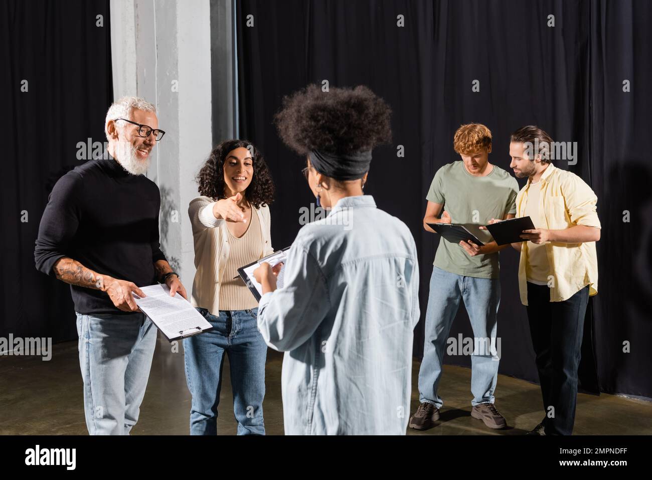smiling multiracial woman pointing with hand near bearded art director ...