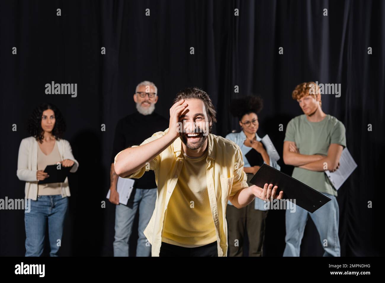 laughing man touching face and looking at camera near blurred ...