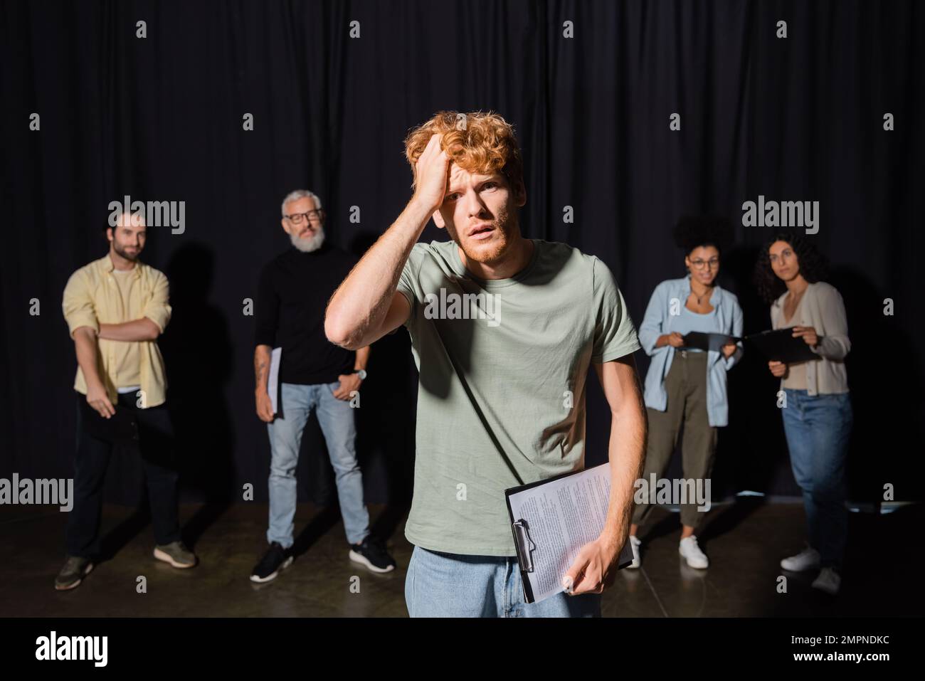 frustrated redhead man holding clipboard and touching head while ...