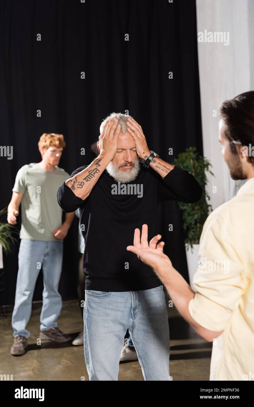 frustrated art director with closed eyes touching head near blurred ...