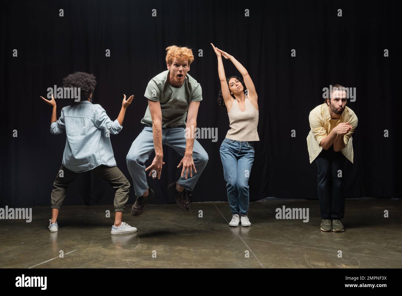 excited redhead man jumping near multiethnic actors posing during ...