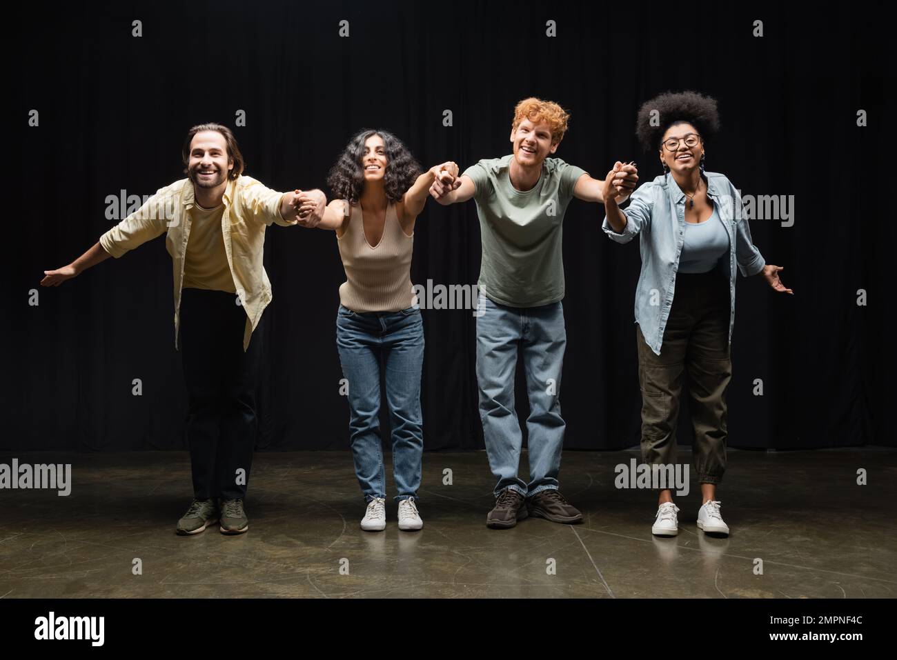 full length of happy multiethnic actors holding hands and bowing on ...