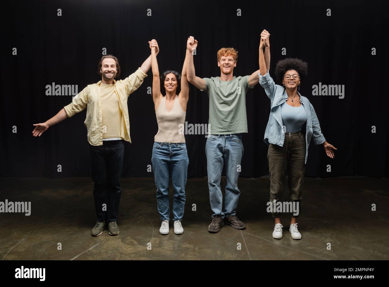 full length of young and joyful interracial actors holding raised hands ...