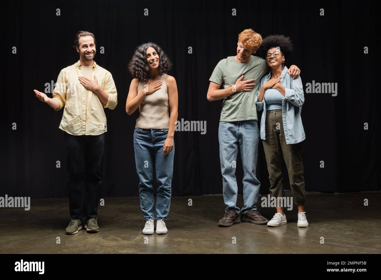 full length of pleased multicultural actors holding hands on chest ...