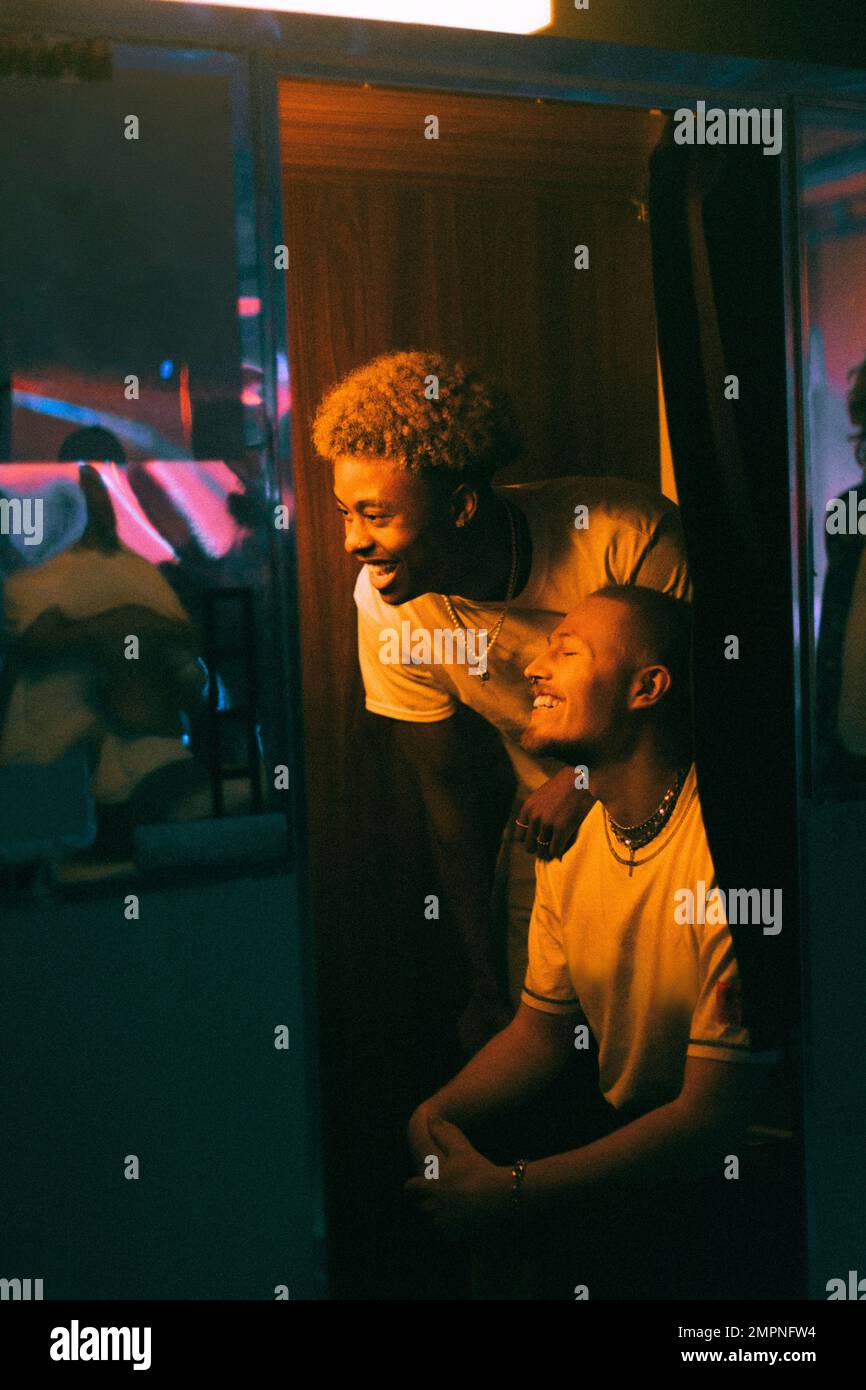 Happy male friends enjoying inside photo booth in illuminated club ...