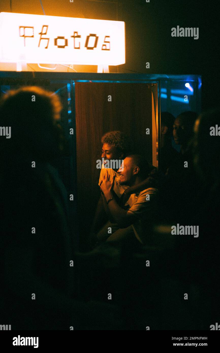 Happy multiracial friends enjoying inside photo booth in illuminated ...