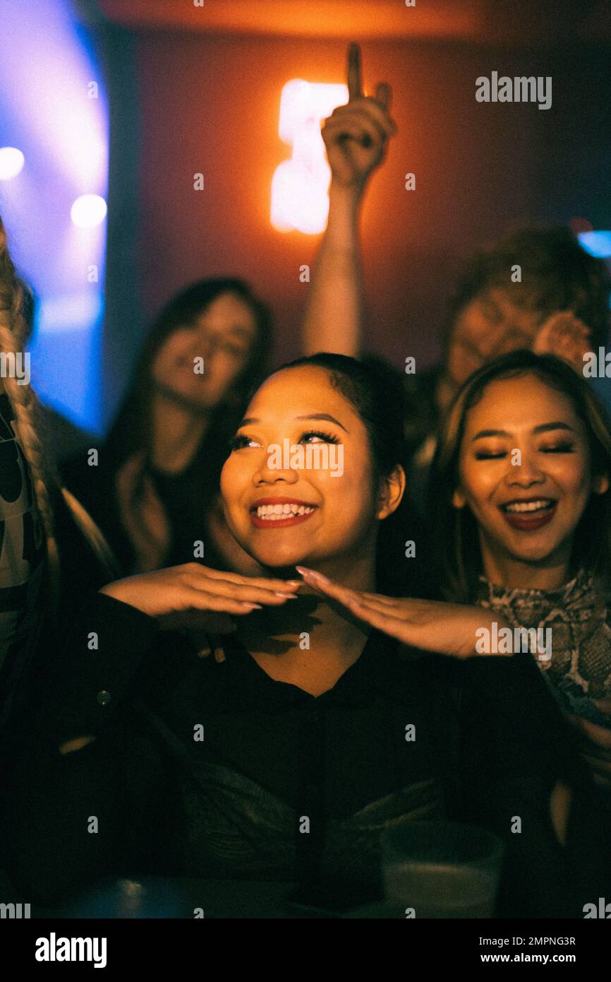 Happy young woman enjoying while dancing with friends in club at night ...