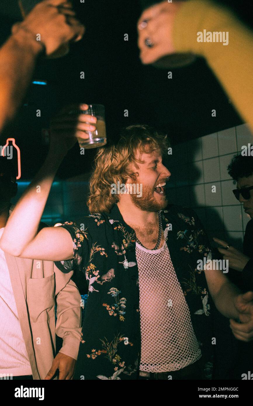 Cheerful young man holding drink dancing with friends at nightclub ...
