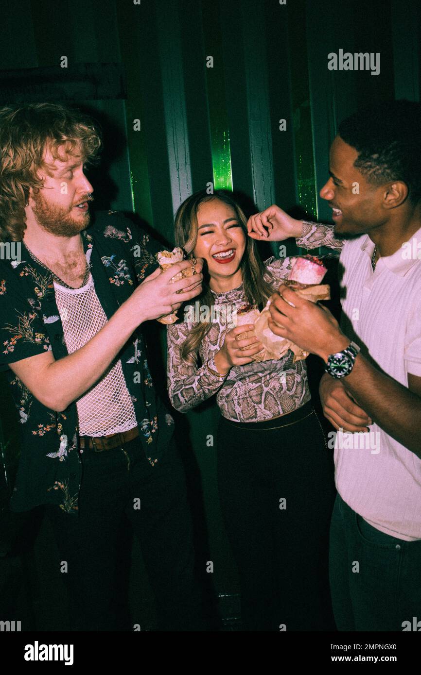 Cheerful young multiracial friends eating wrap sandwiches together at ...