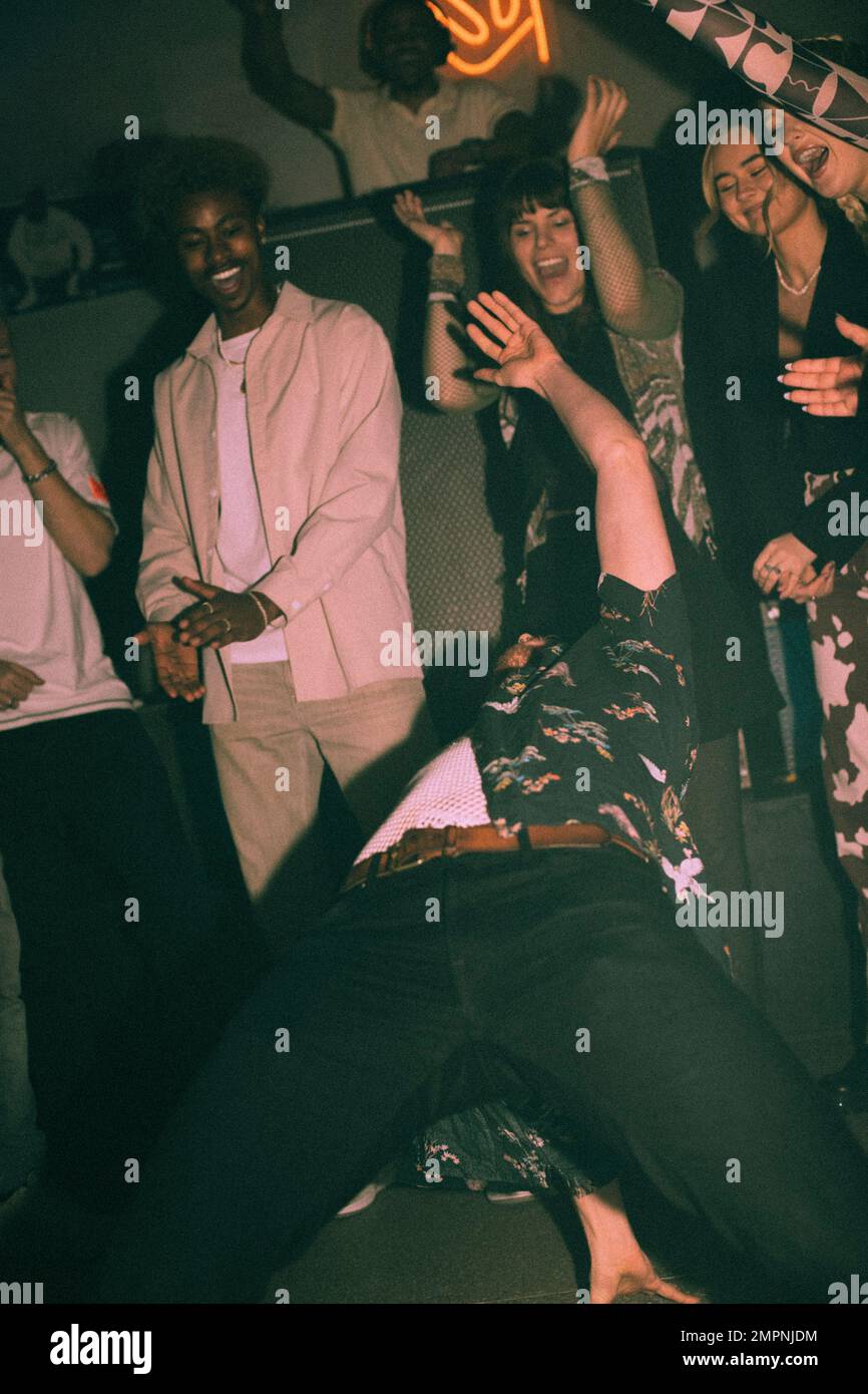 Young men and women cheering friend dancing while bending backwards at ...