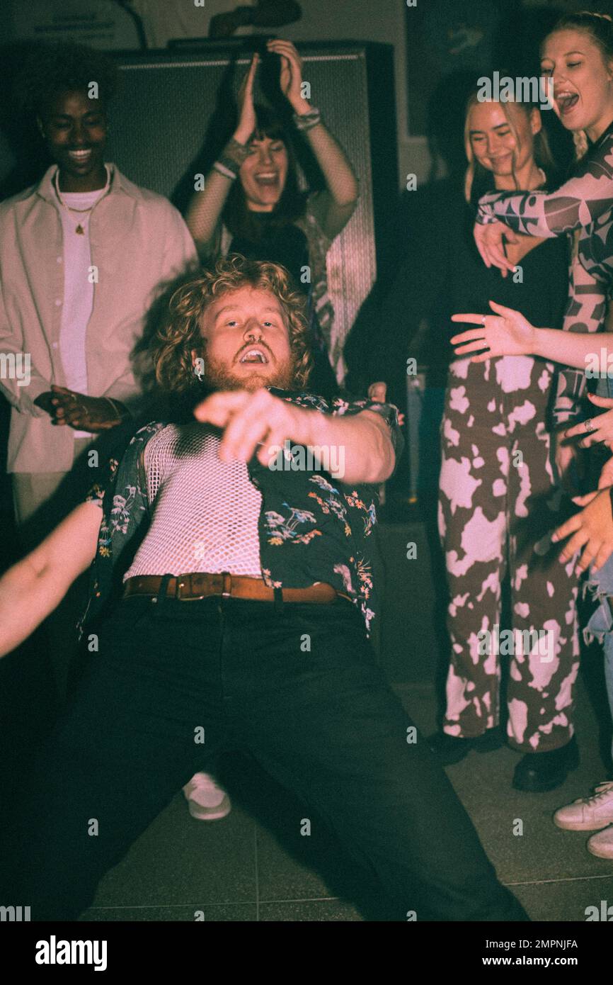 Portrait of flexible young man bending backwards dancing amidst friends ...